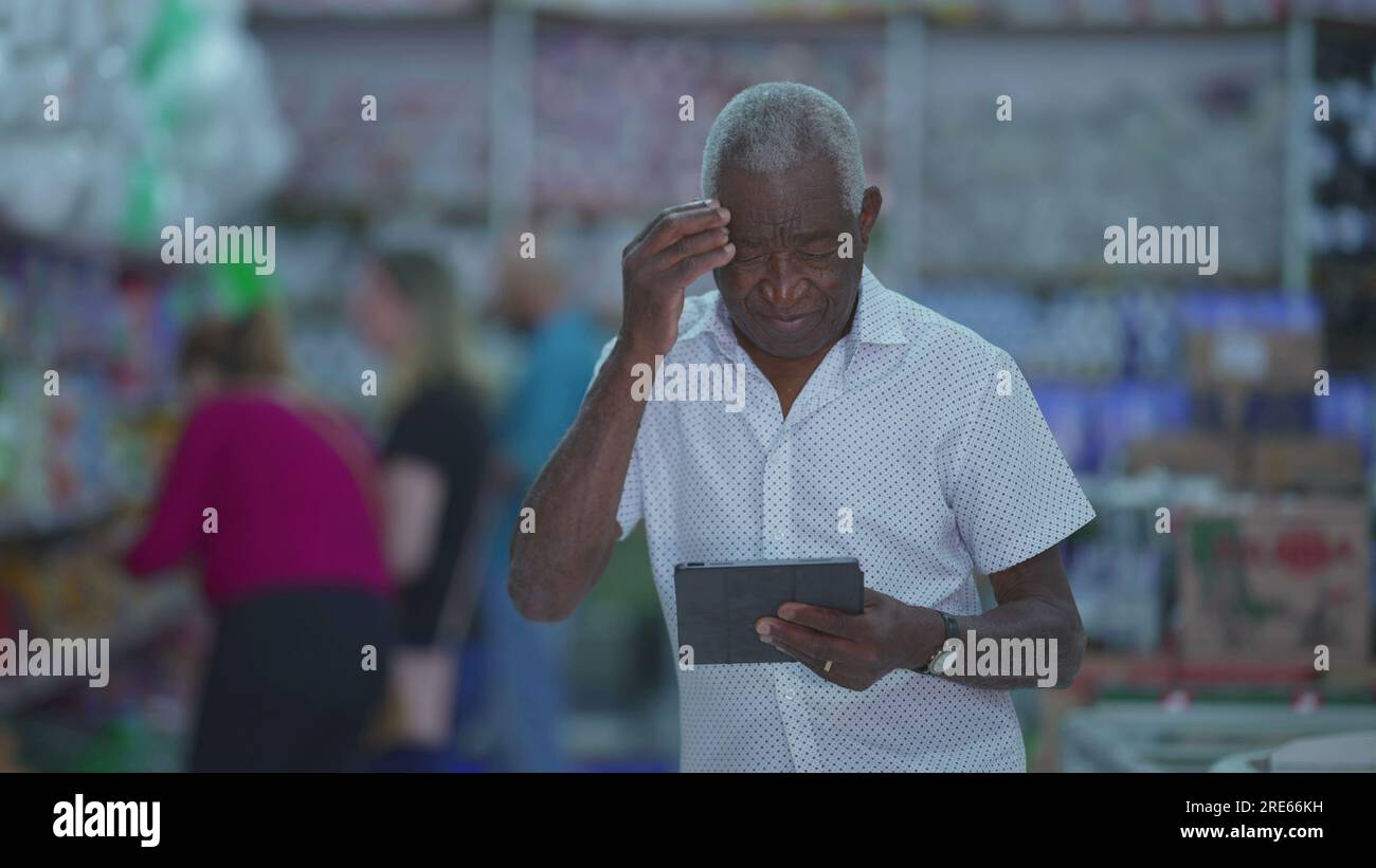 Confused senior man using tablet device inside small business store ...