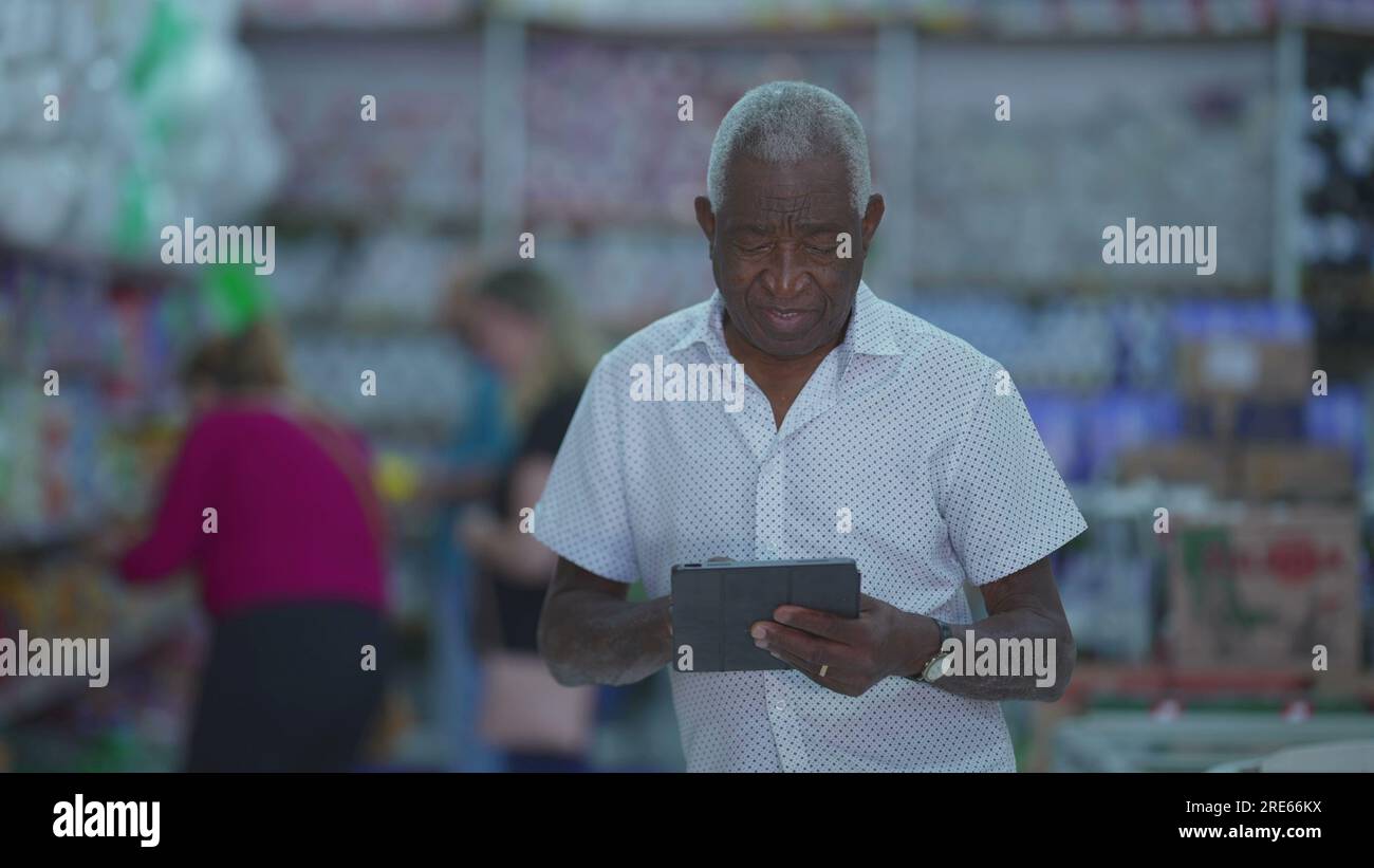 Confused senior man using tablet device inside small business store ...