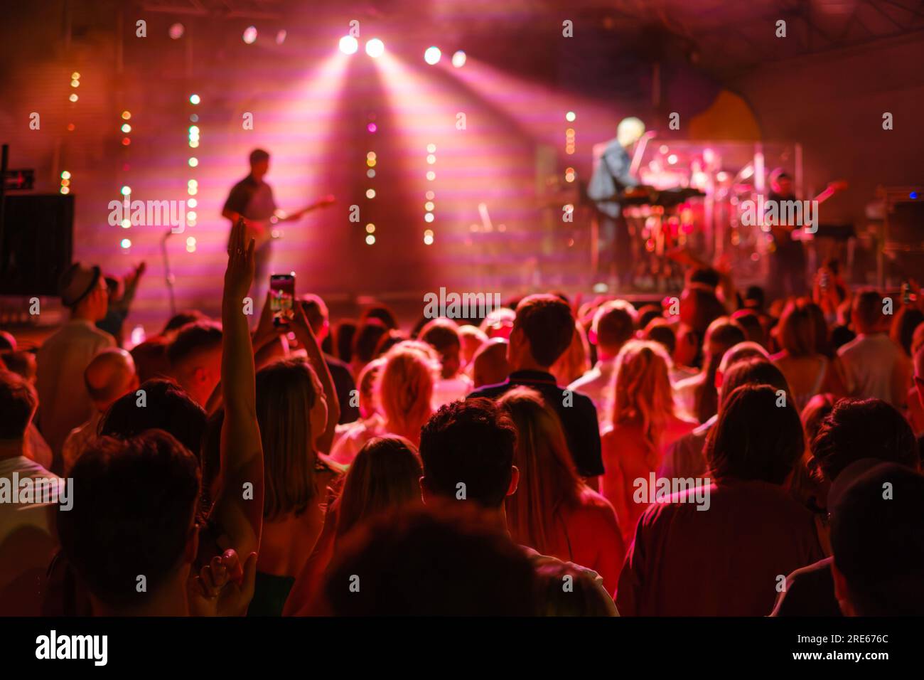 Back view of anonymous crowd enjoying live music show on stage in neon ...