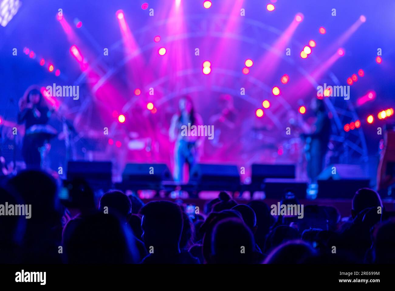 Crowd of fans near stage with performing music band in glowing red ...