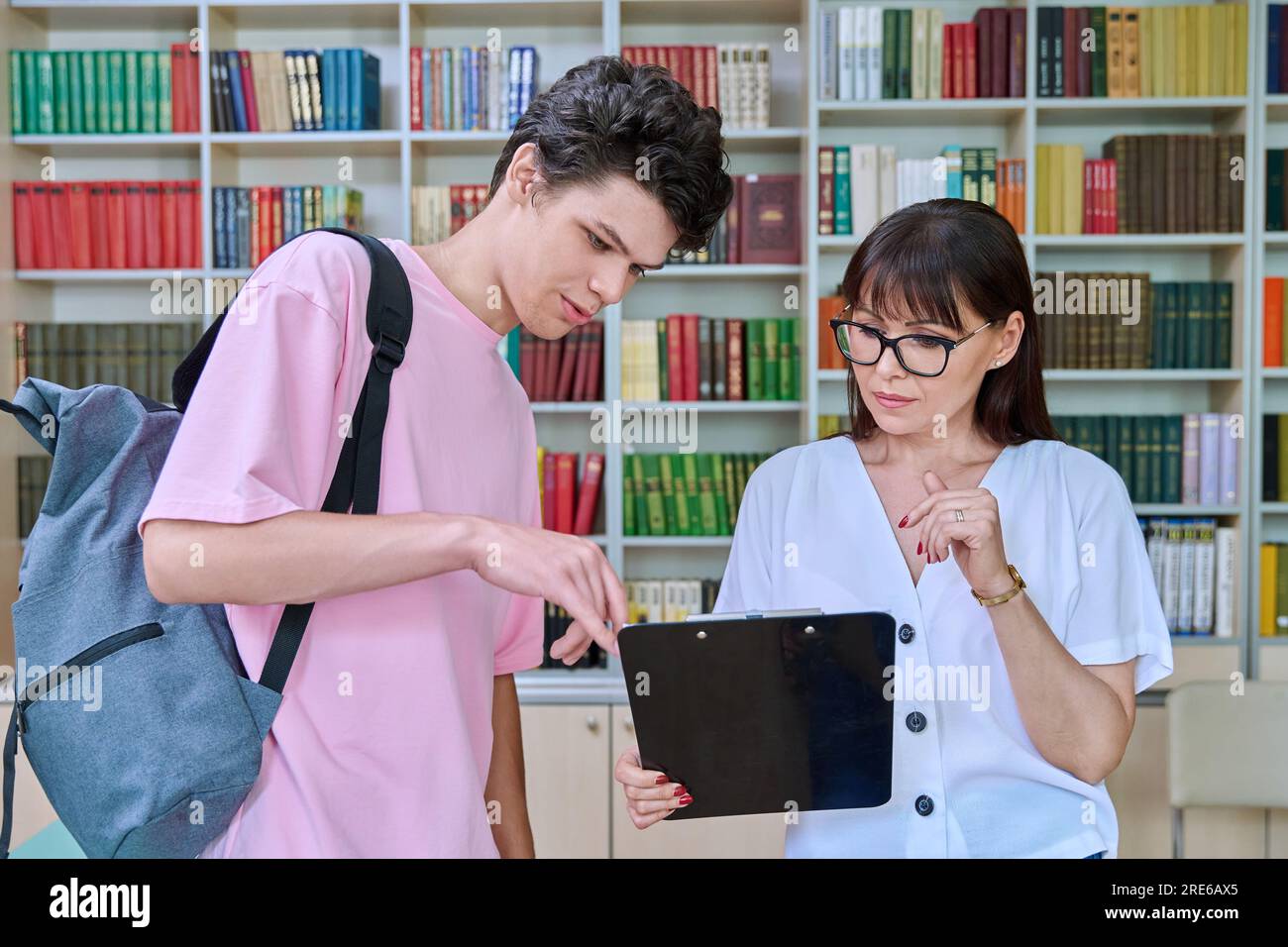 Middle-aged female teacher talking to male college student inside library Stock Photo - Alamy