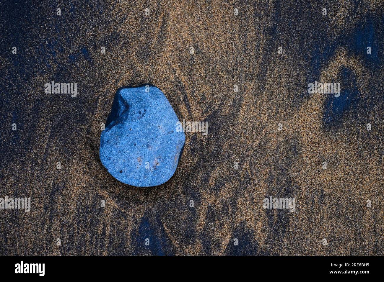 A single large blue stone isolated on background of volcanic beach sand ...