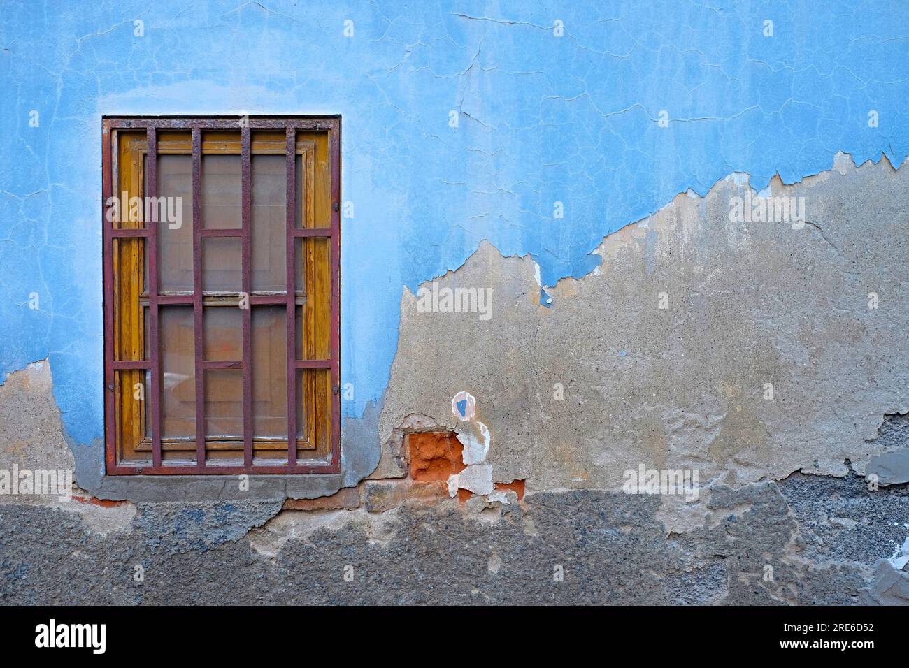 A simple barred wooden window in an old weathered wall with blue ...