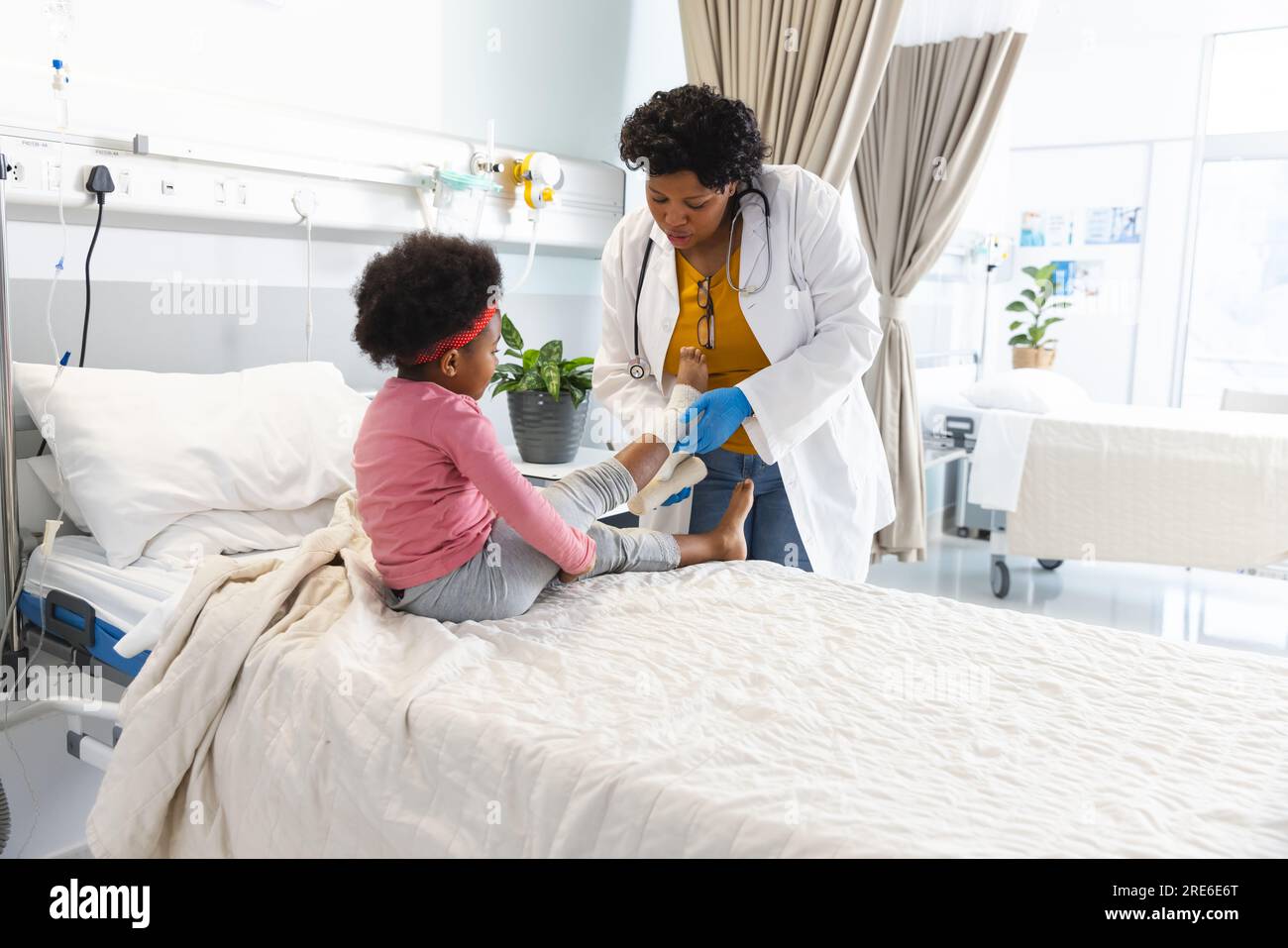African american female doctor dressing girl patient leg with bandage ...