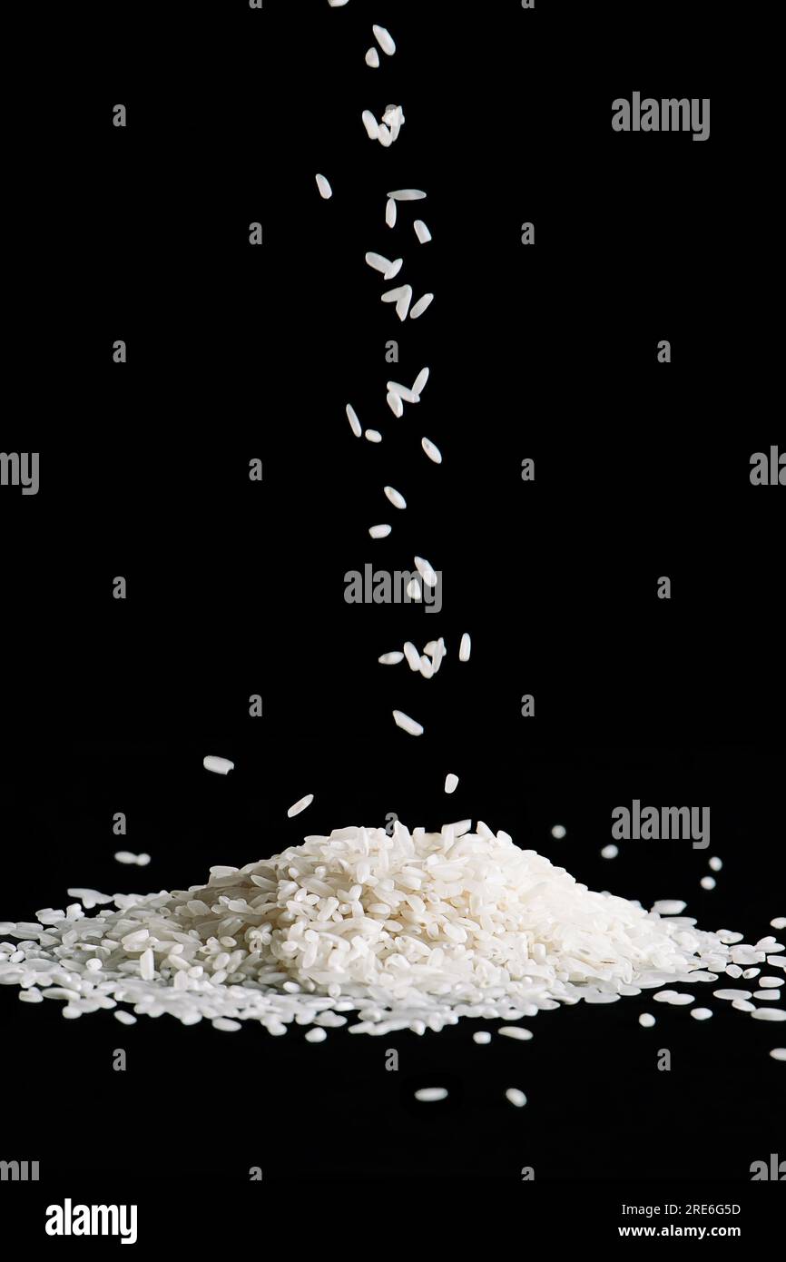 Raw white rice is falling on table. Pile of uncooked long rice on black ...
