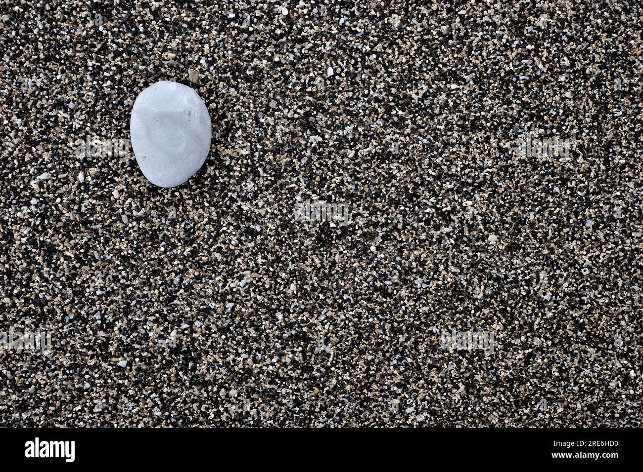One isolated oval pale white stone on rough pebble background, offset ...