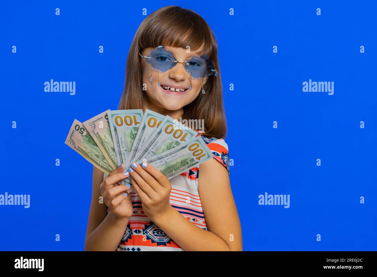 Rich pleased young cute school girl waving money dollar cash banknotes ...