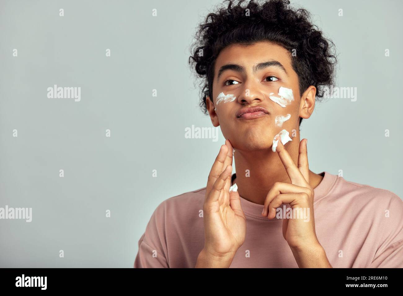 Studio portrait of handsome smiling guy with black curly hair applying ...