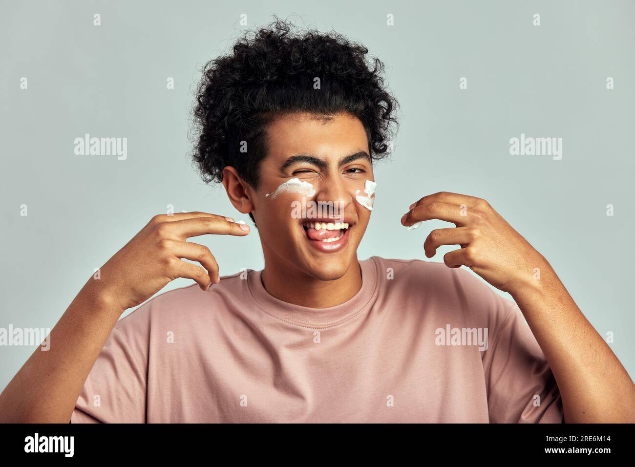 Studio portrait of handsome smiling guy with black curly hair applying ...