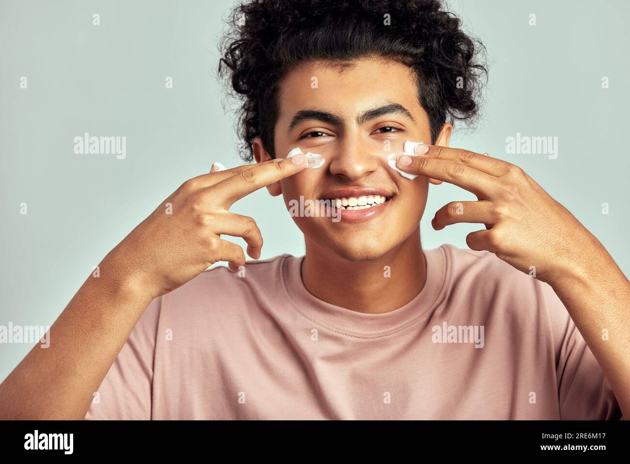 Studio portrait of handsome smiling guy with black curly hair applying ...