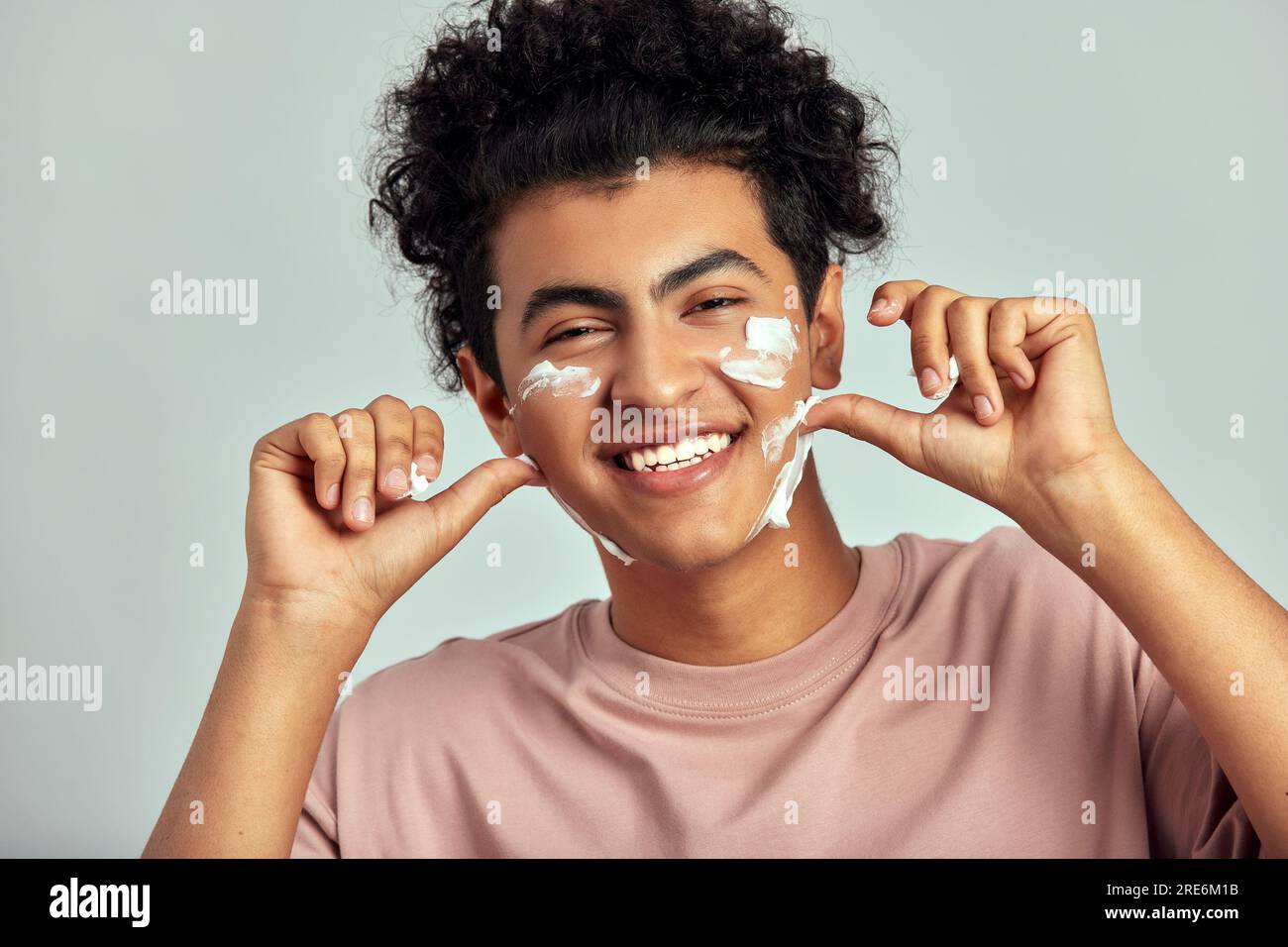 Studio portrait of handsome smiling guy with black curly hair applying ...