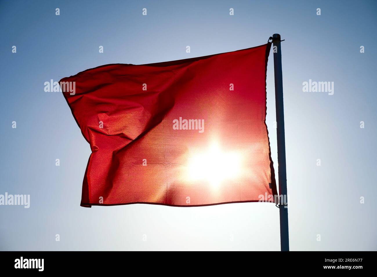 A red flag backlit with bright sun rays, isolated on bright blue sky ...