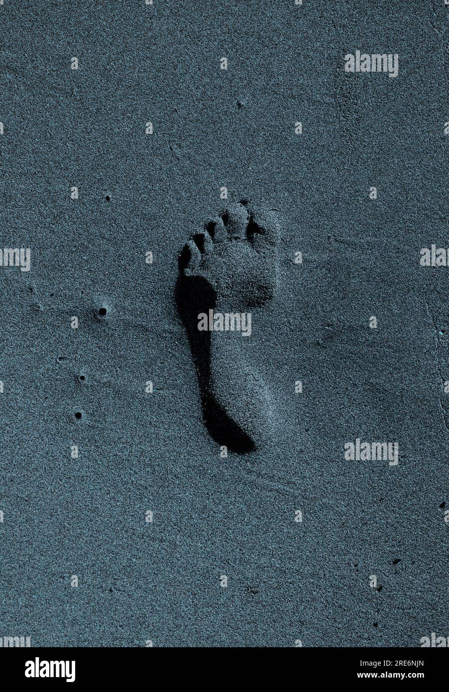A signle isolated footprint in the sand, centered and lit by the ...
