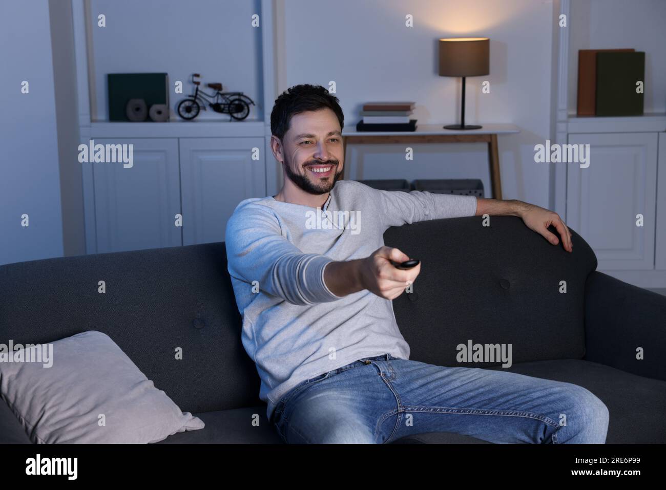 Happy man changing TV channels with remote control on sofa at home ...