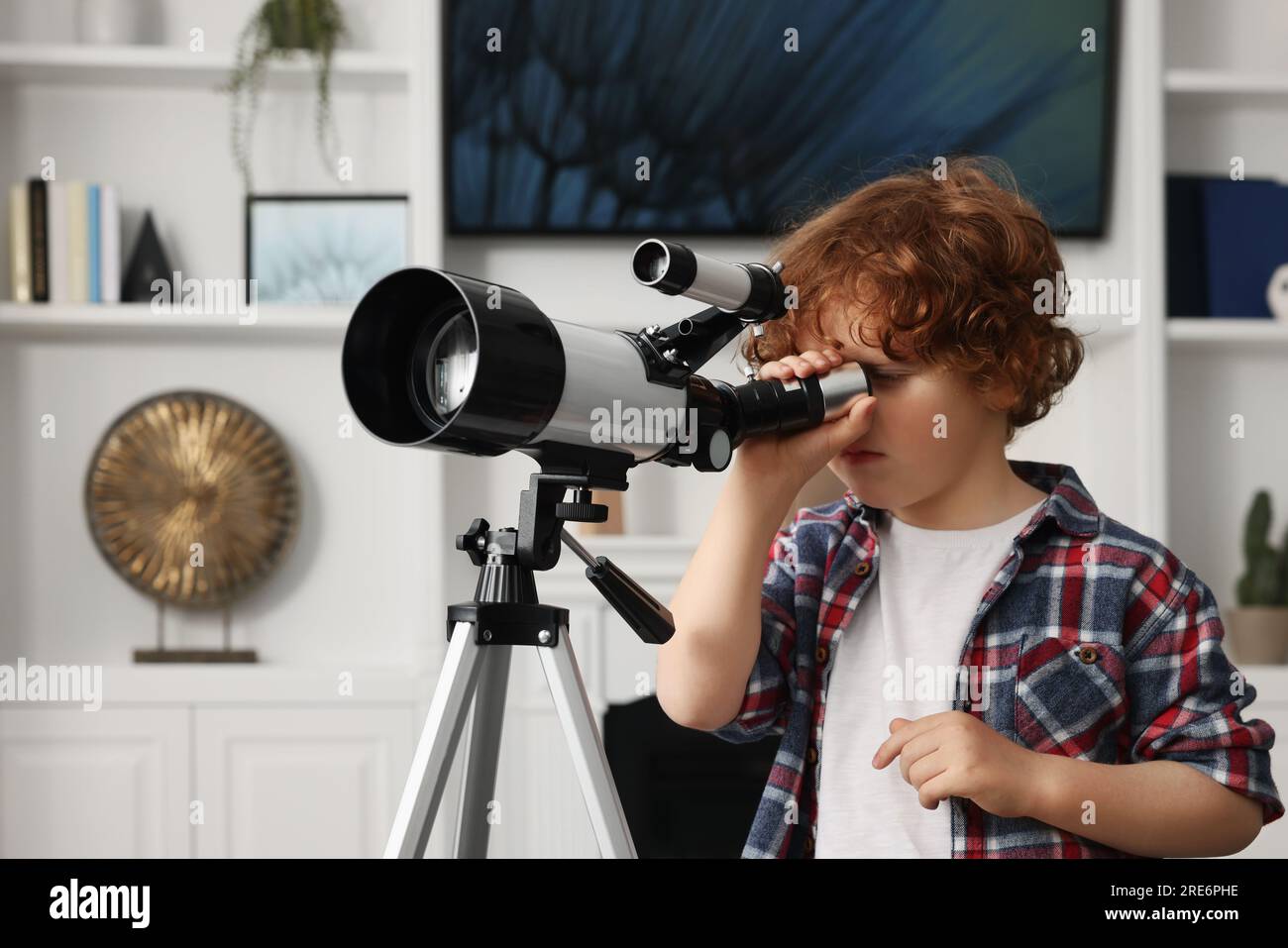 Cute little boy looking at stars through telescope in room Stock Photo ...