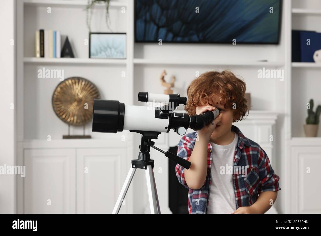 Cute little boy looking at stars through telescope in room Stock Photo ...