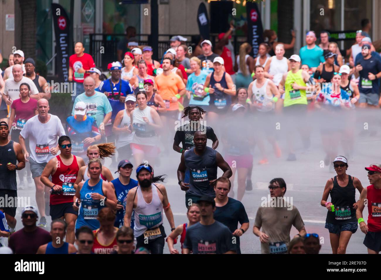 Atlanta, GA / USA – July 4, 2023: Runners run through a cooling mist ...