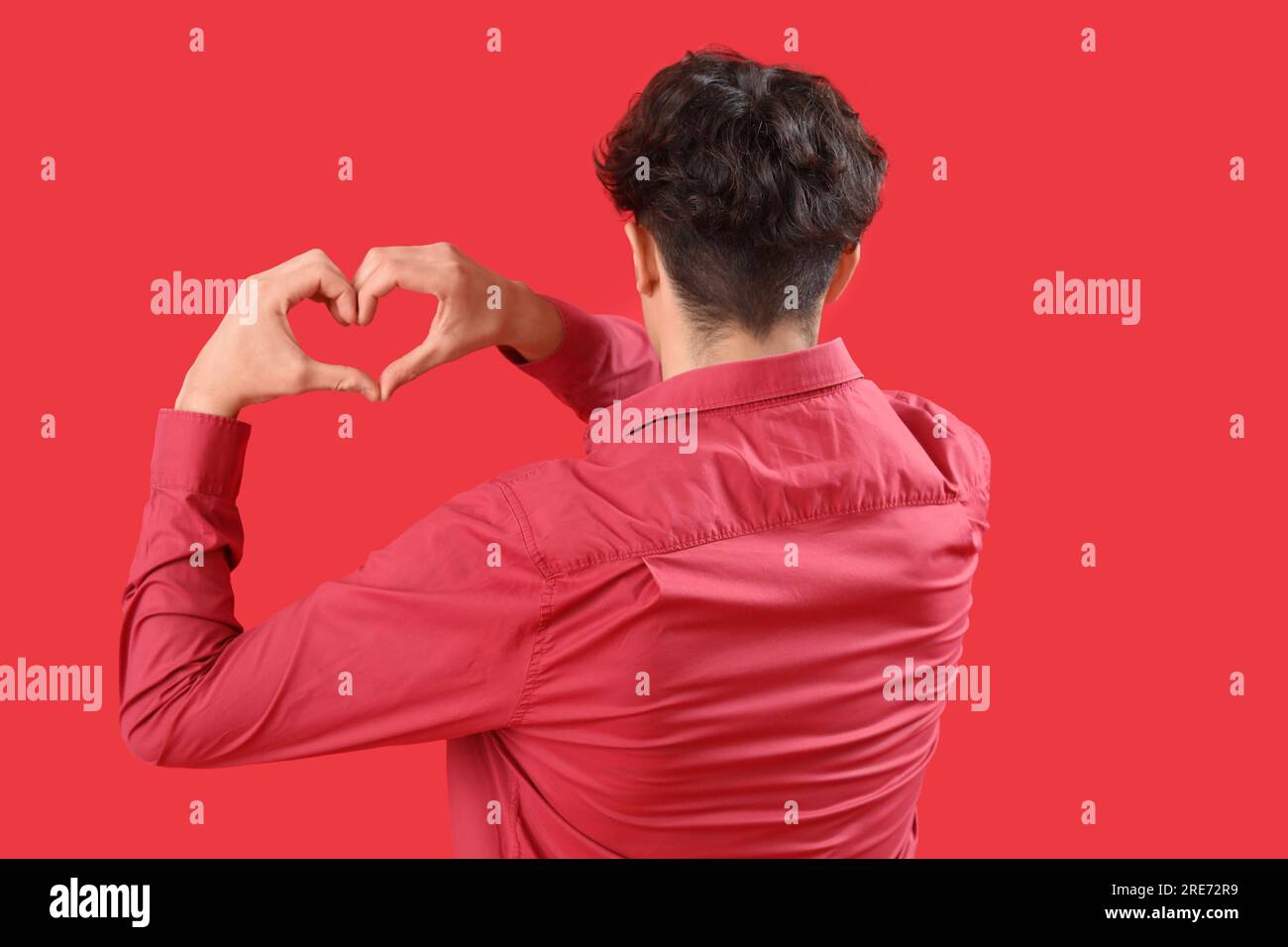 Handsome young man making heart with his hands on red background, back ...