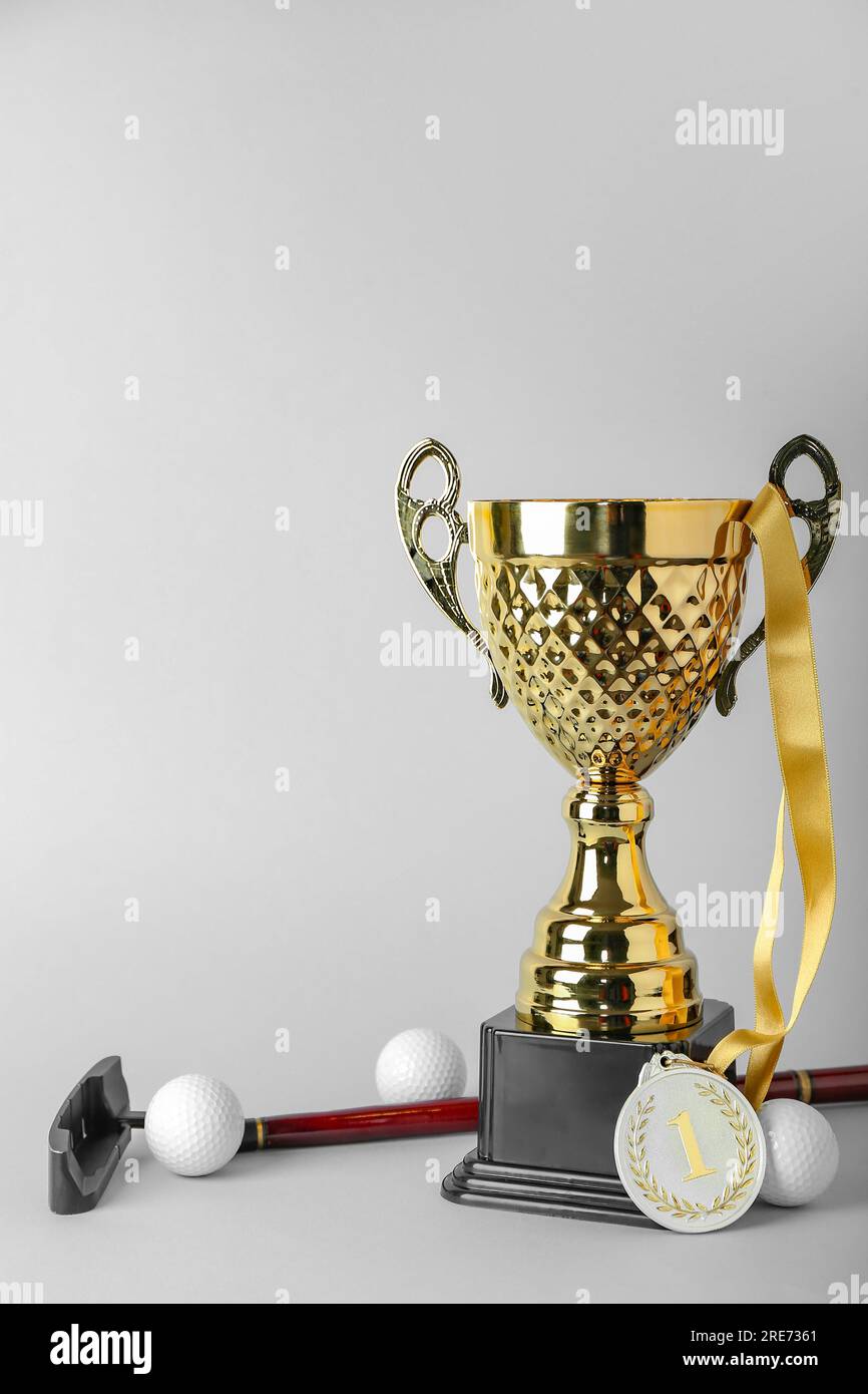 Gold cup with first place medal, golf club and balls on light ...