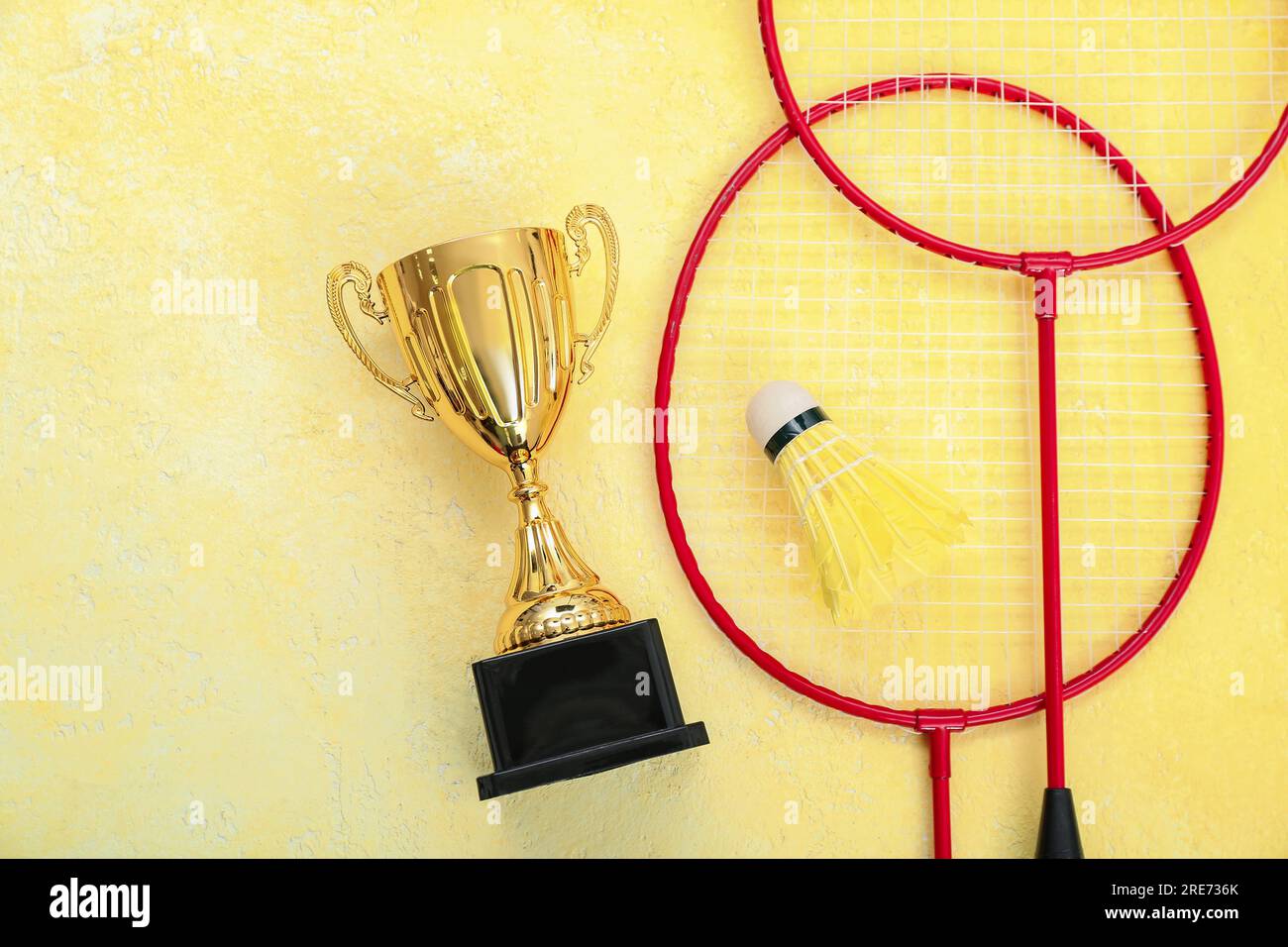 Gold cup with badminton rackets and shuttlecock on yellow background ...