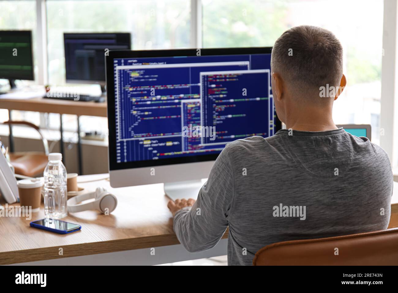 Mature male programmer sitting in light office at his workplace, back ...
