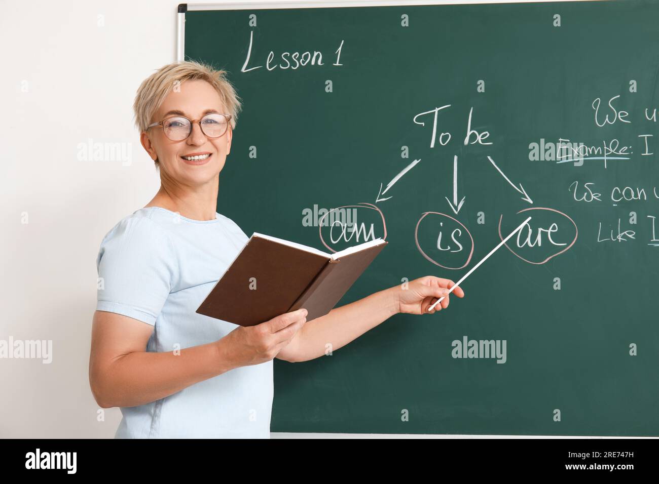 Female English teacher with book conducting grammar lesson in classroom ...