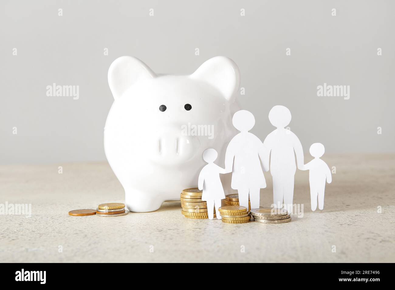 Figures of family with piggy bank and coins on light table. Savings ...