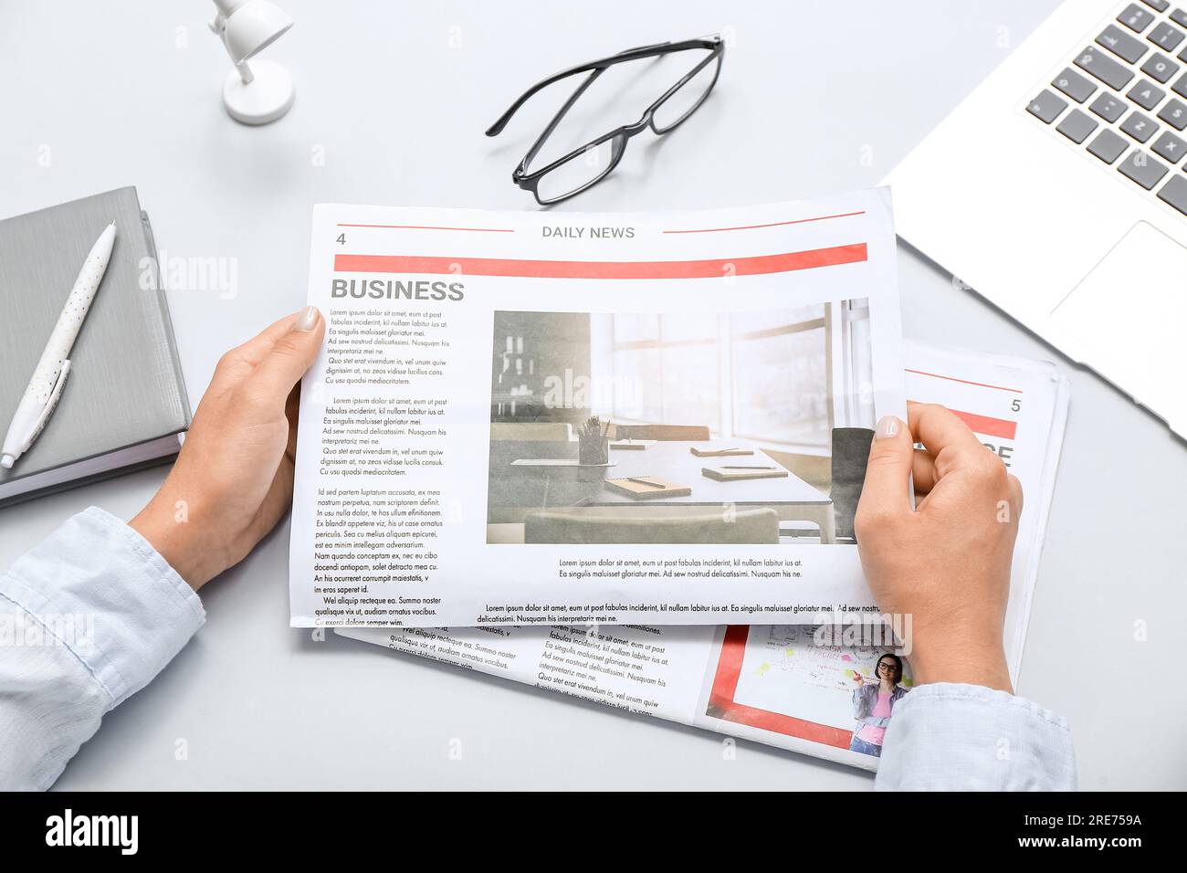 Woman reading newspaper at workplace with laptop and eyeglasses on grey ...