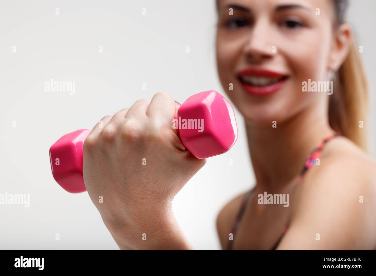 A blurred woman lifts small, pink weights in focus. Her light workout ...