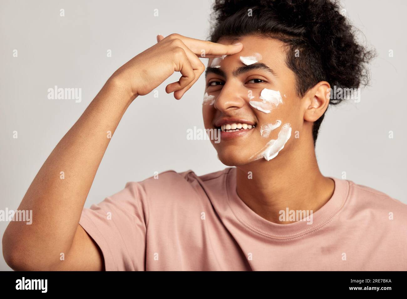 Studio portrait of handsome smiling guy with black curly hair applying ...