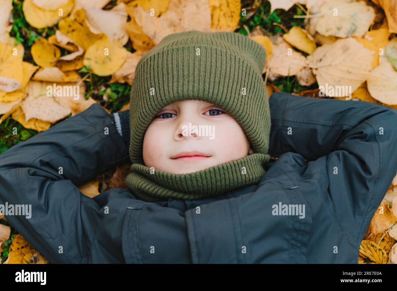 cute little boy laying on ground covered with yellow fallen leaves ...