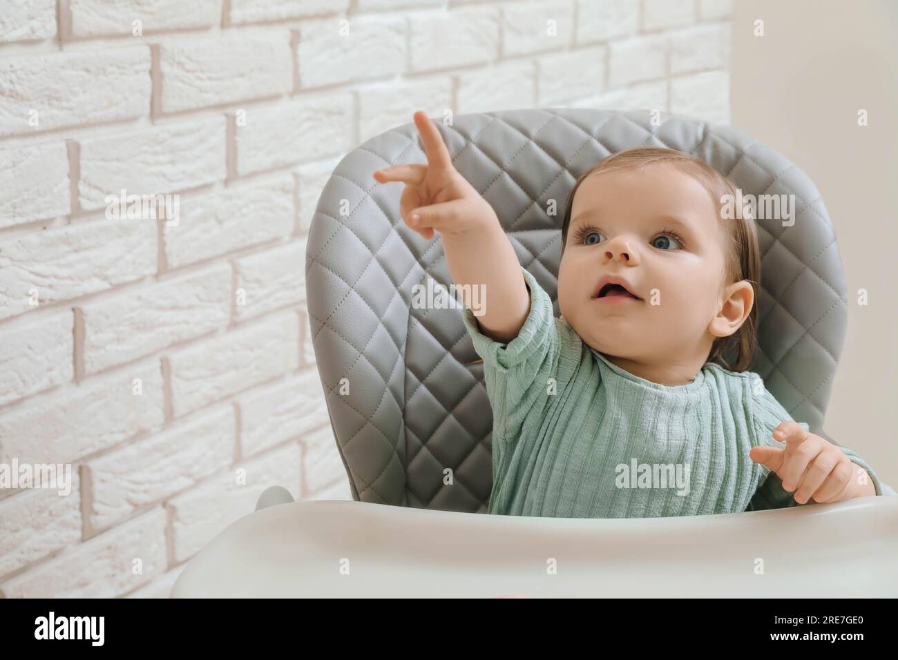 Cute little baby pointing at something in high chair indoors. Space for ...