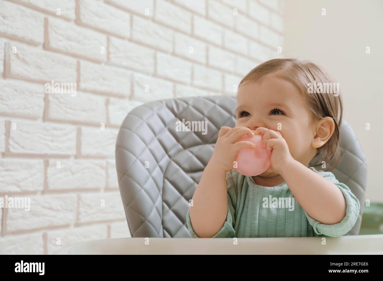 Cute little baby nibbling toy in high chair indoors. Space for text ...