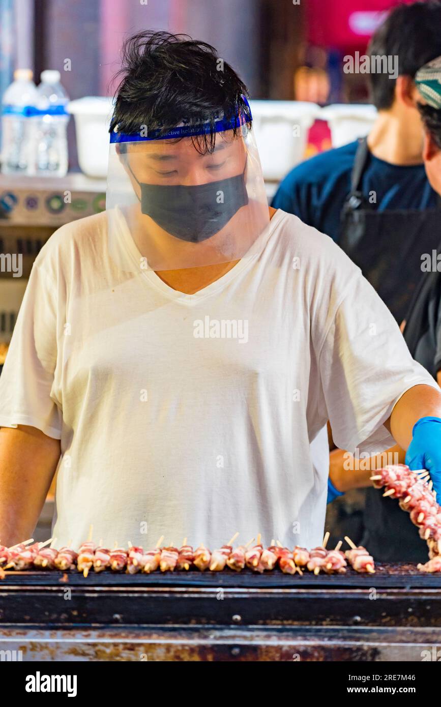 A person wearing a cloth and plastic shield mask while cooking ...
