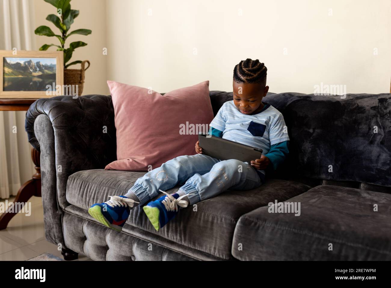 Happy african american boy sitting on couch using tablet in living room ...