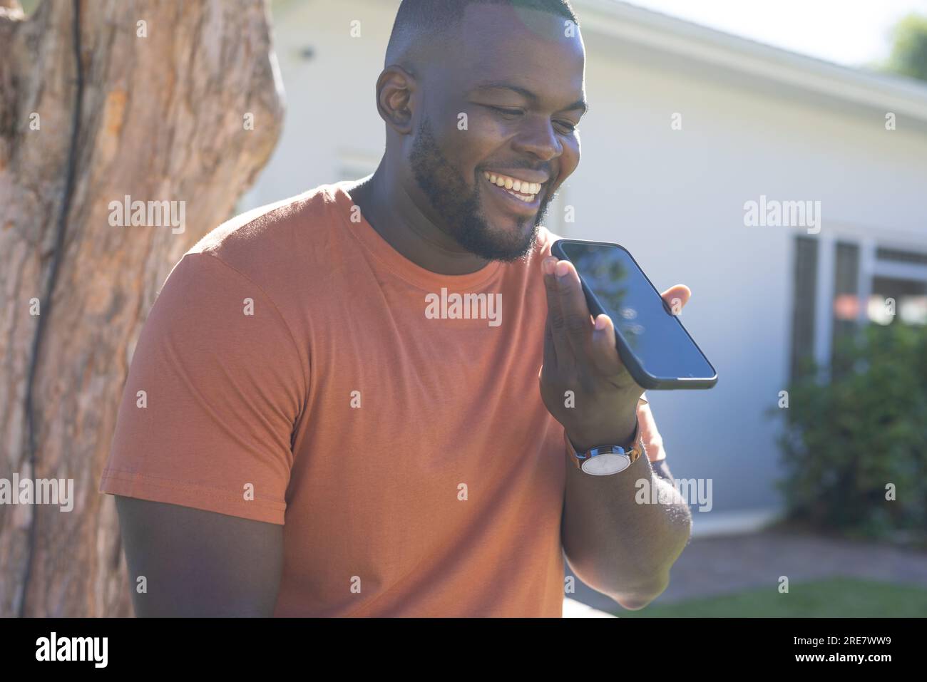 Happy african american talking on smartphone sitting in sunny garden ...