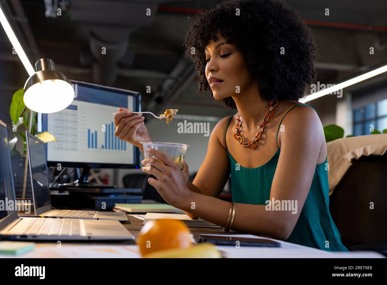 African american woman having a snack sitting on her desk at office ...