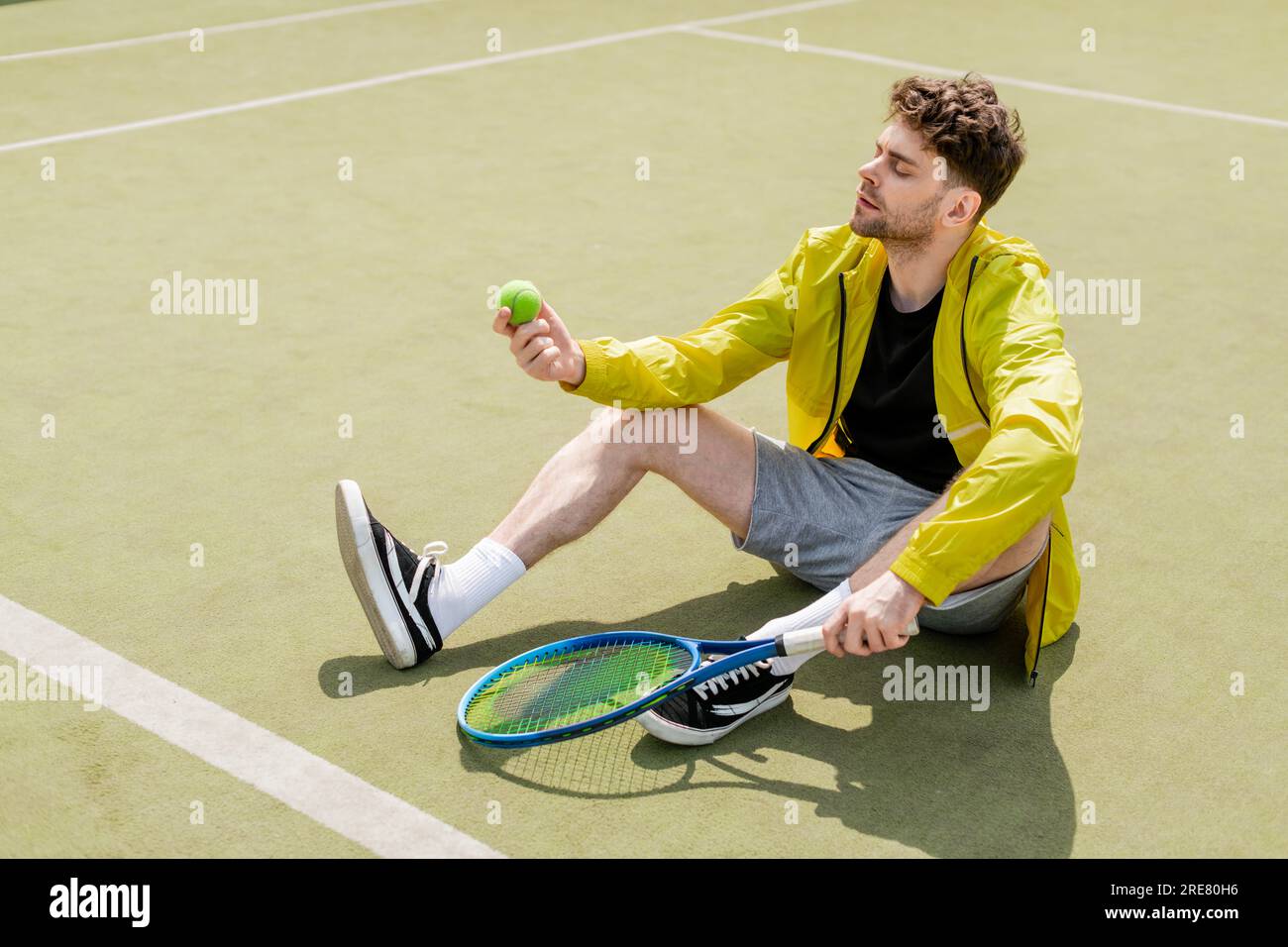 male tennis player sitting on court and holding racket, looking at ...