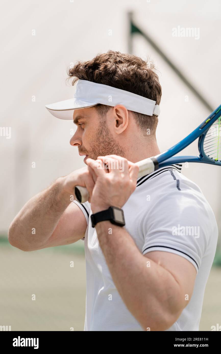 handsome tennis player in sports visor holding racket on court ...