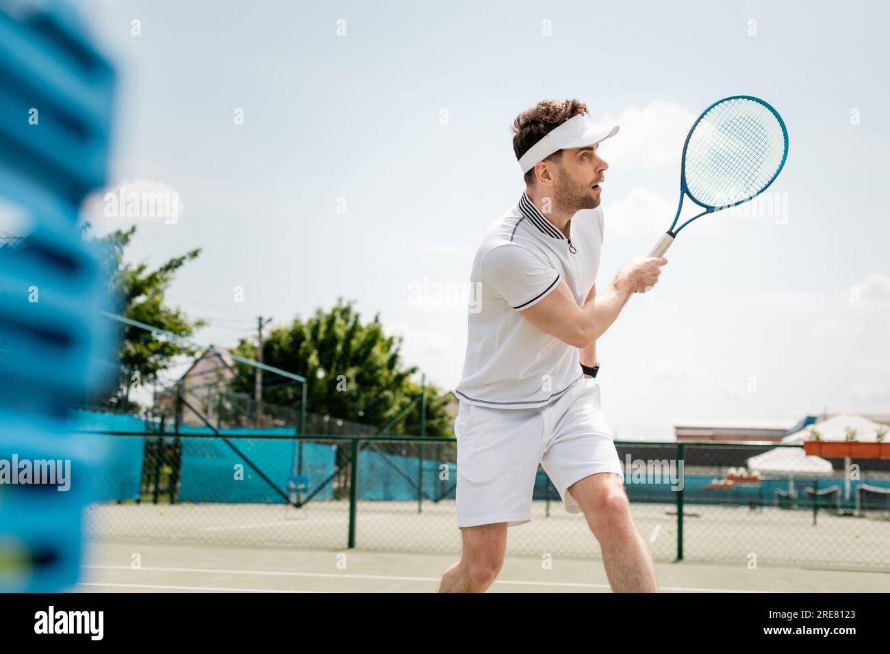 handsome tennis player in sports visor holding racket and playing ...