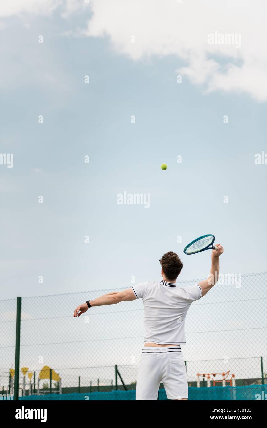 back view of man playing tennis on court, holding racket, hitting ball ...