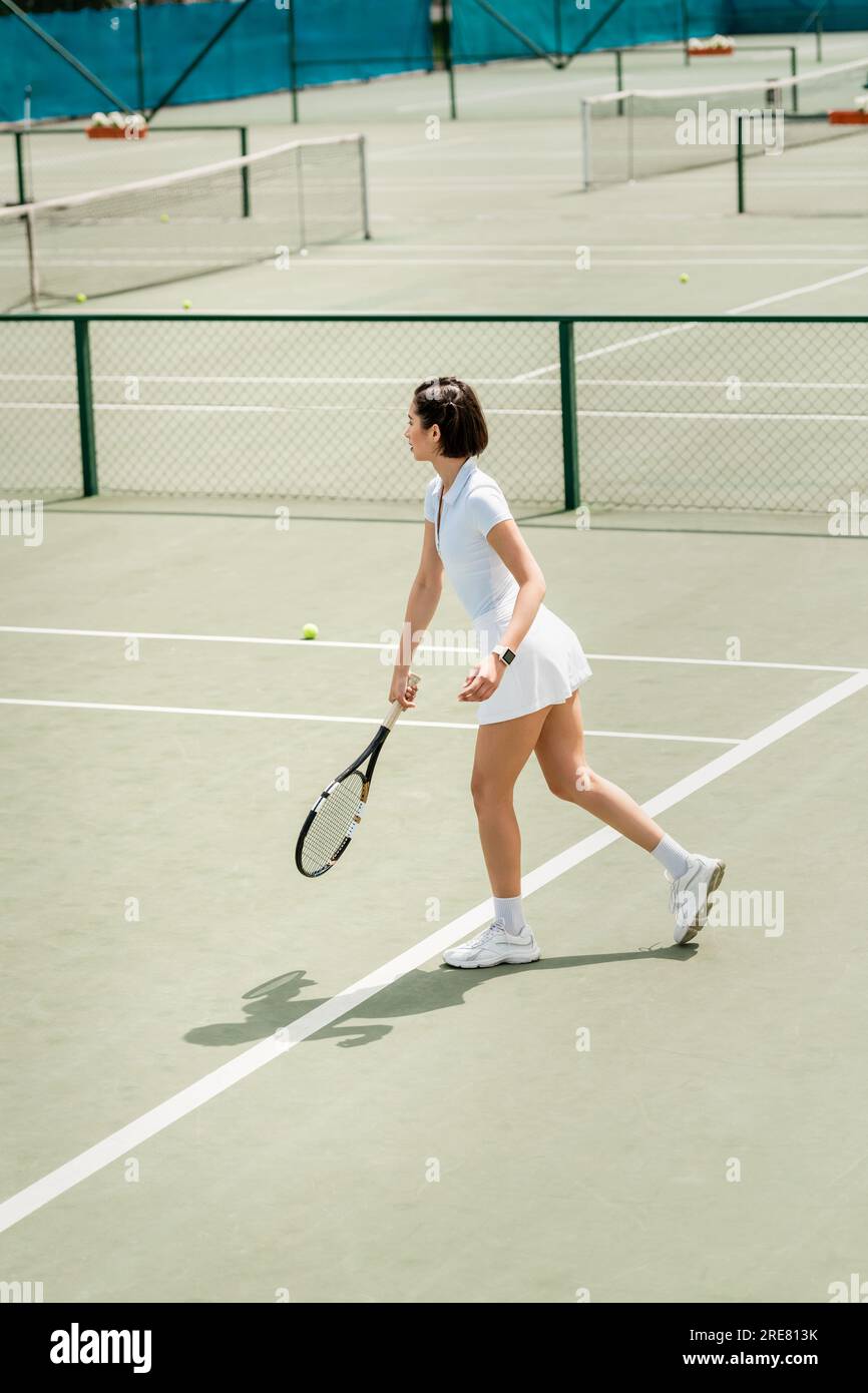 side view, sportswoman in white active wear holding racket on tennis ...