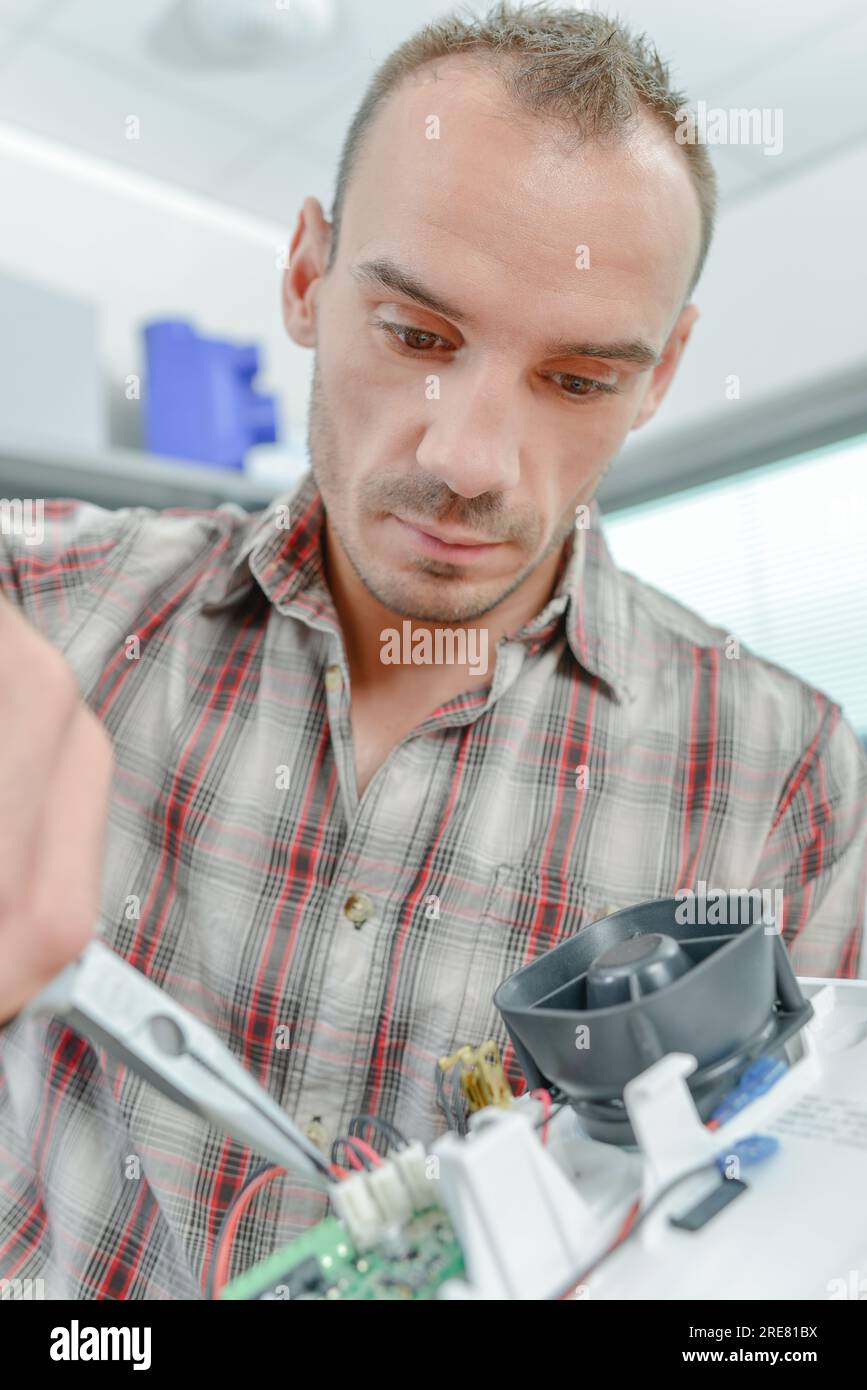 Man repairing back of electrical device with fan using long nosed ...