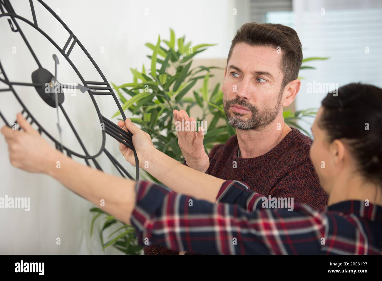 happy man and woman putting a clock on the wall Stock Photo - Alamy