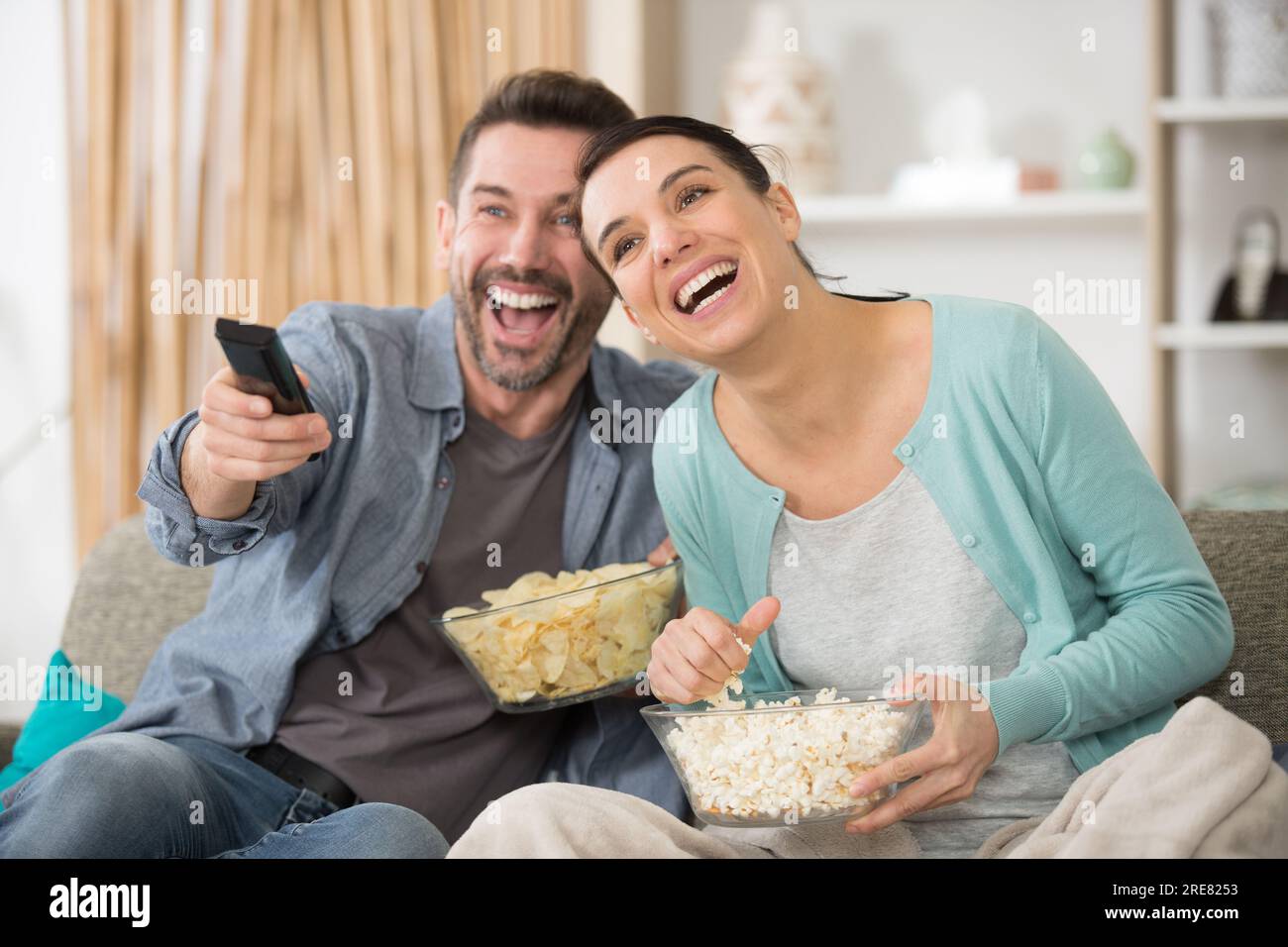 couple laughing and eating snacks while watching tv Stock Photo - Alamy