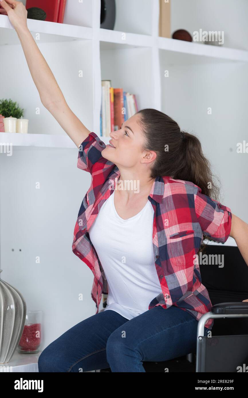 woman in wheelchair reaching for something from living-room shelf Stock ...