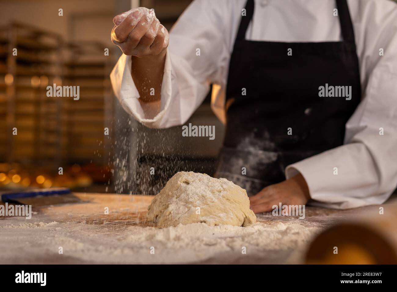 Asian female baker wearing apron in bakery kitchen and pouring flour on ...