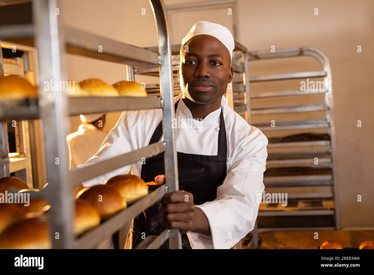 Focused african american male baker in bakery kitchen with baking trays ...
