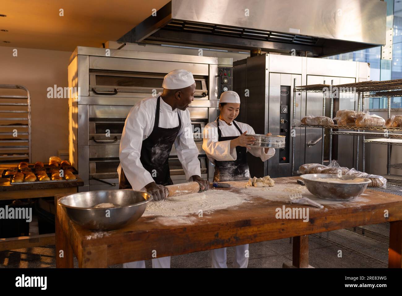 Happy diverse bakers wearing aprons in bakery kitchen and preparing ...