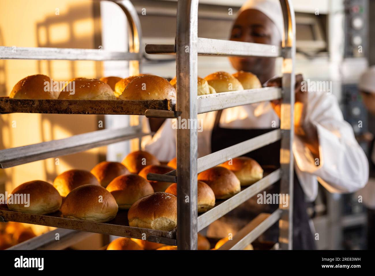 Focused african american male baker in bakery kitchen with baking trays ...
